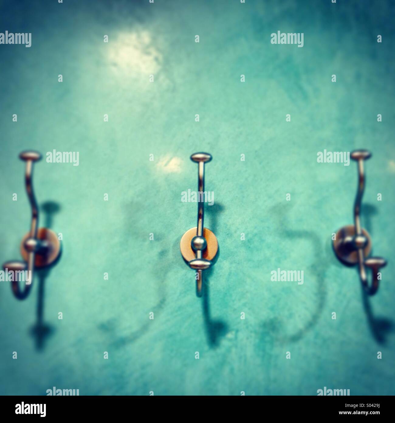 Three empty hooks fixed to a turquoise wall Stock Photo - Alamy