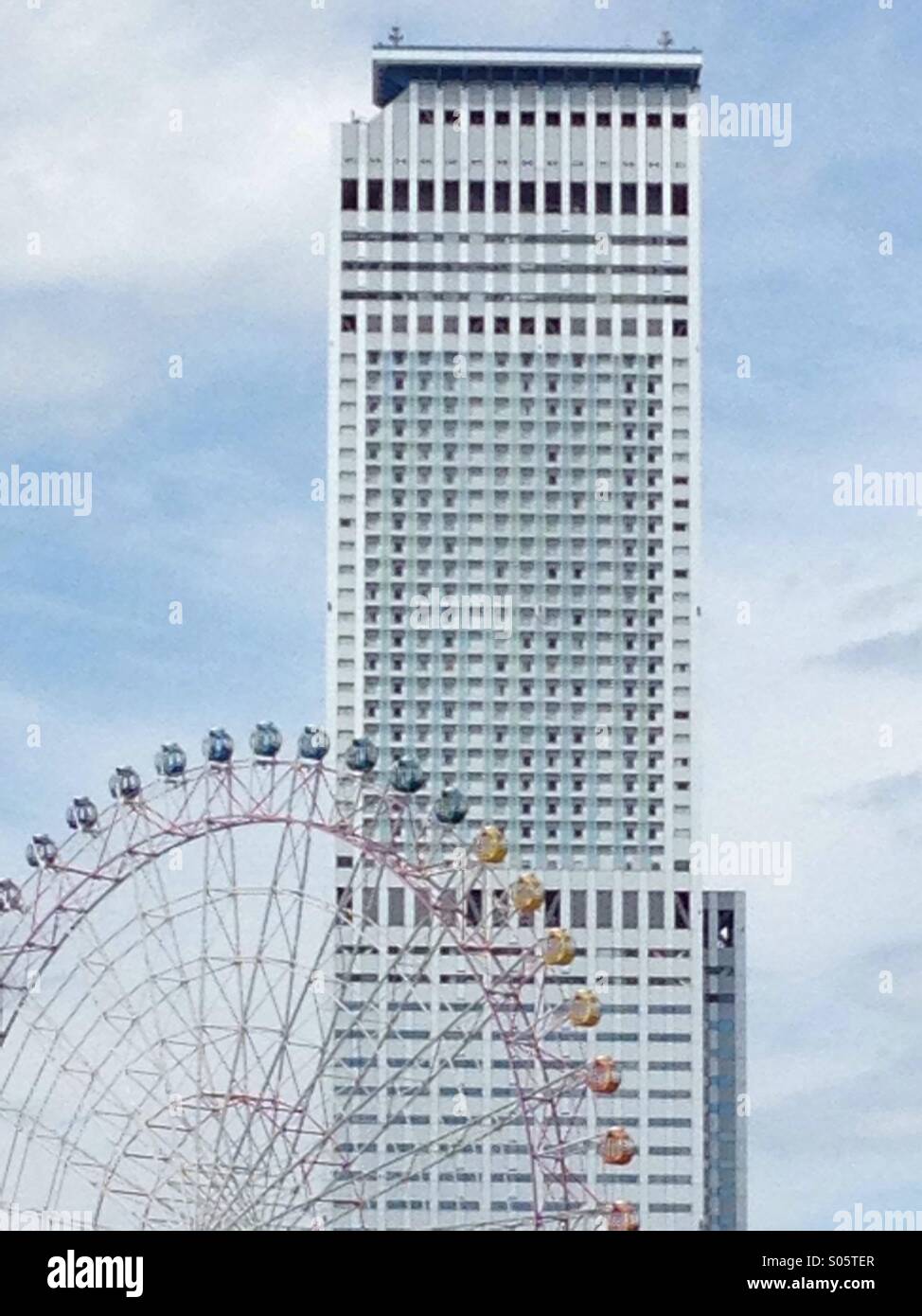 Partial Ferris wheel in front of modern high rise building, sky in ...
