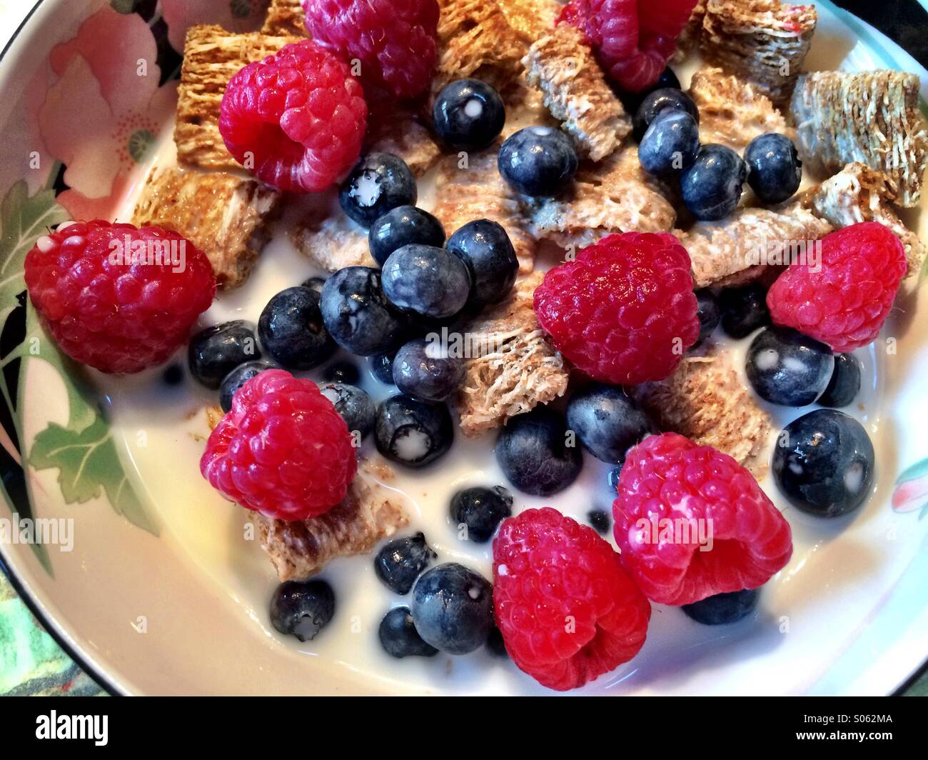 A bowl of whole grain cereal squares with raspberries and blueberries ...