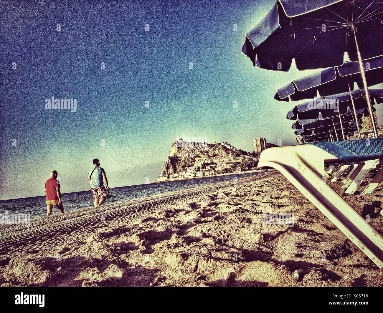 2 men walking ing beach with line of sum umbrellas Stock Photo - Alamy