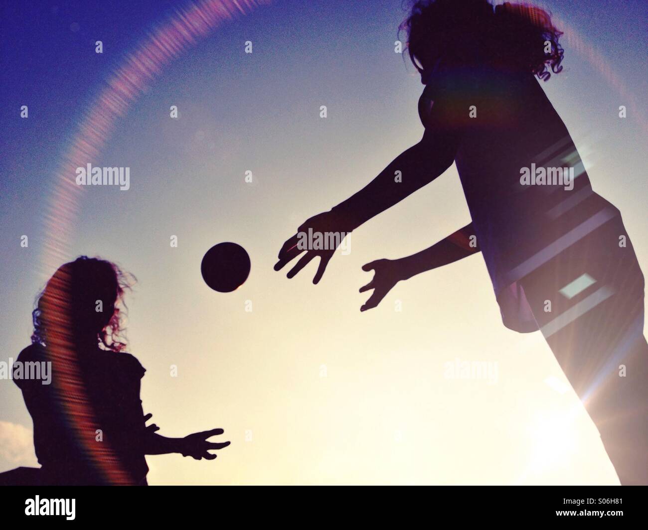 Two girls in silhouette throwing ball between them Stock Photo - Alamy