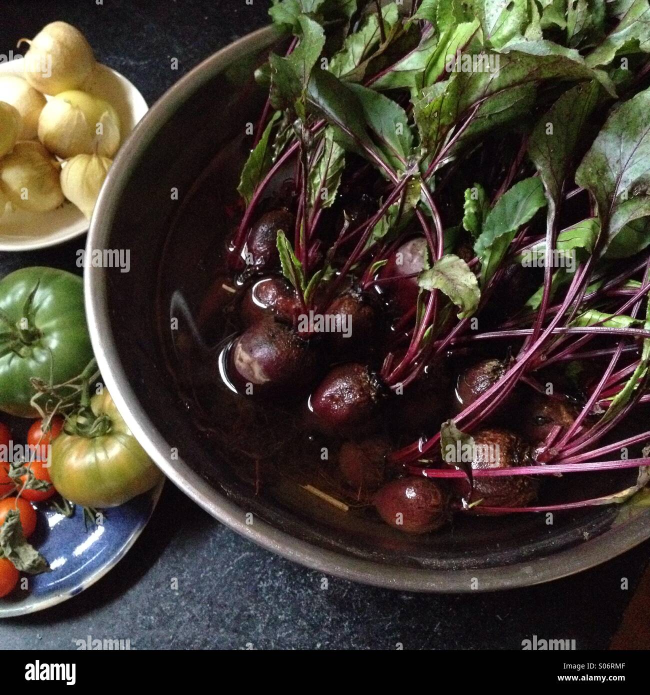Red beets in bowl of water on counter with tomatillos and tomatoes ...