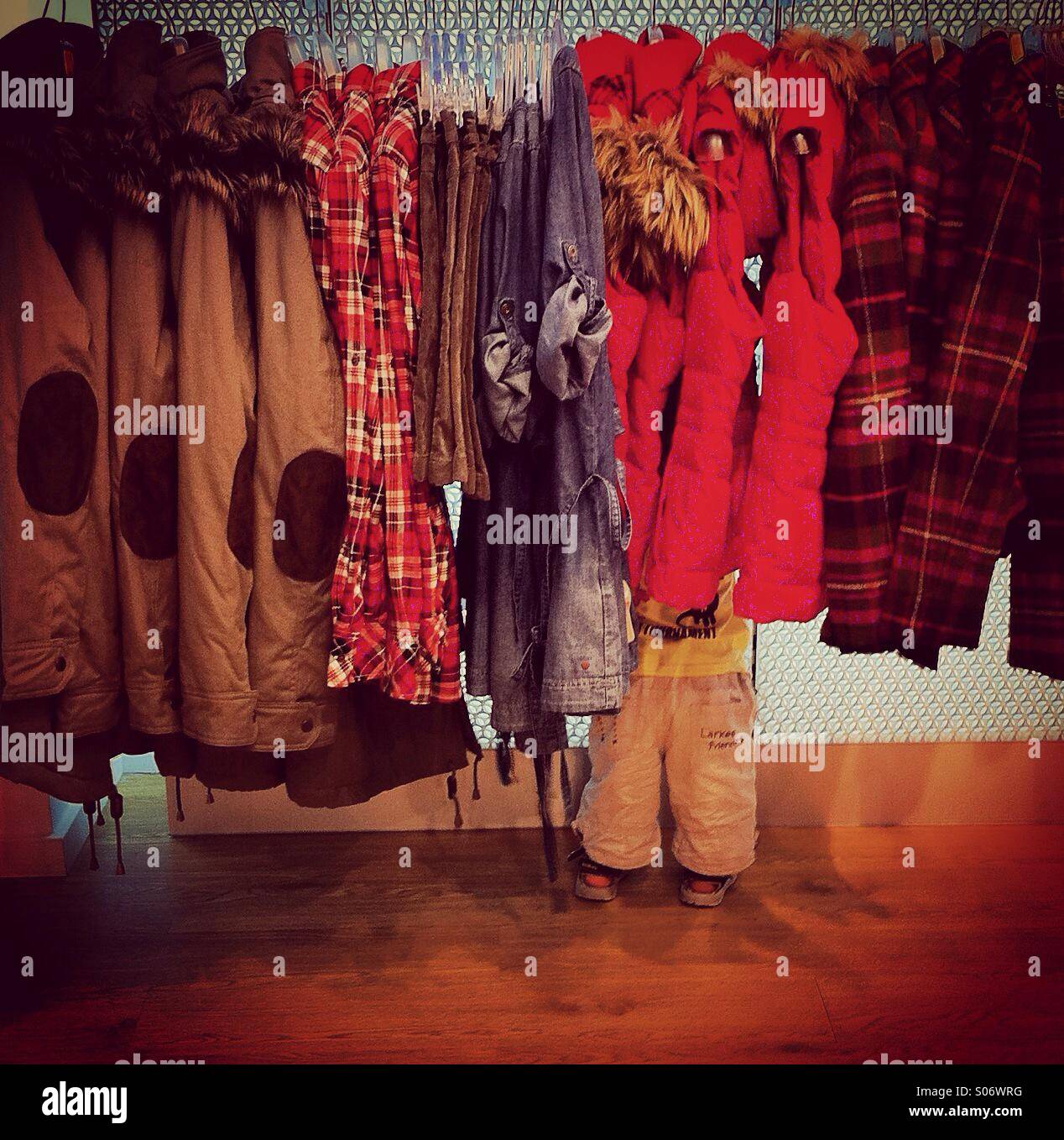 Little child is hidding behind the clothes in a fashion shop Stock ...