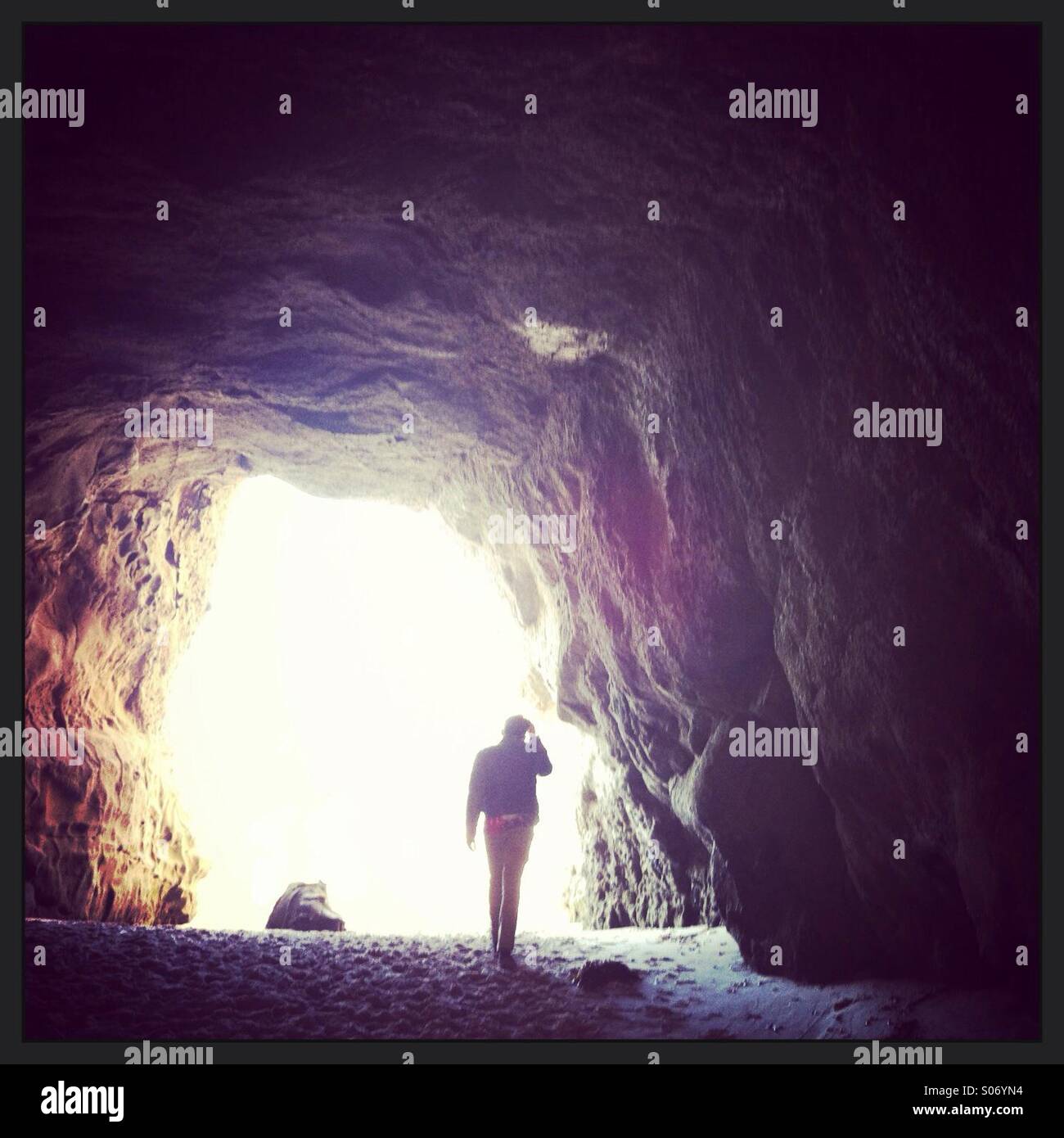 Man walking through cave on beach Stock Photo - Alamy