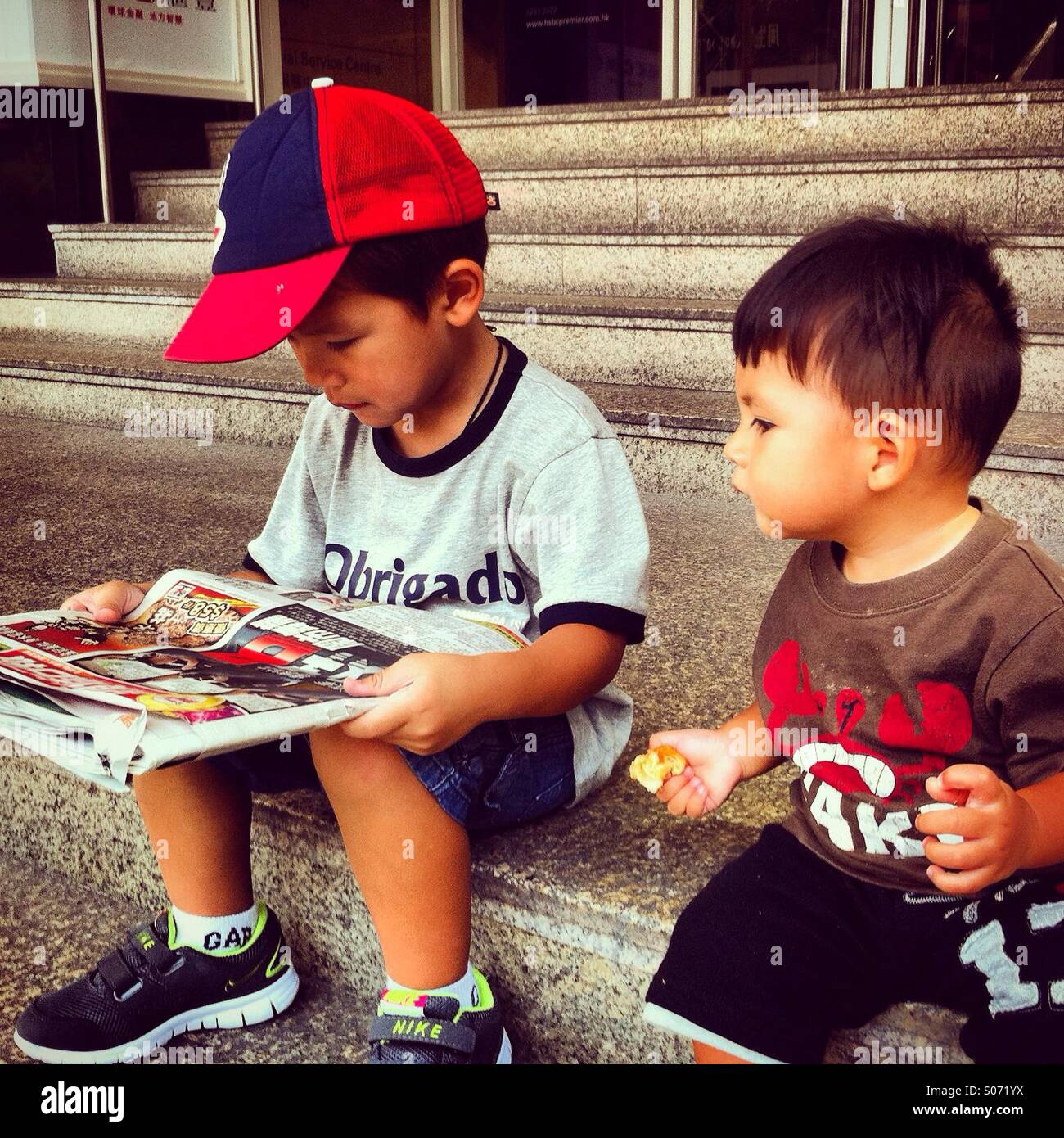 2 brother boys sitting on steps outside and read newspaper Stock Photo ...