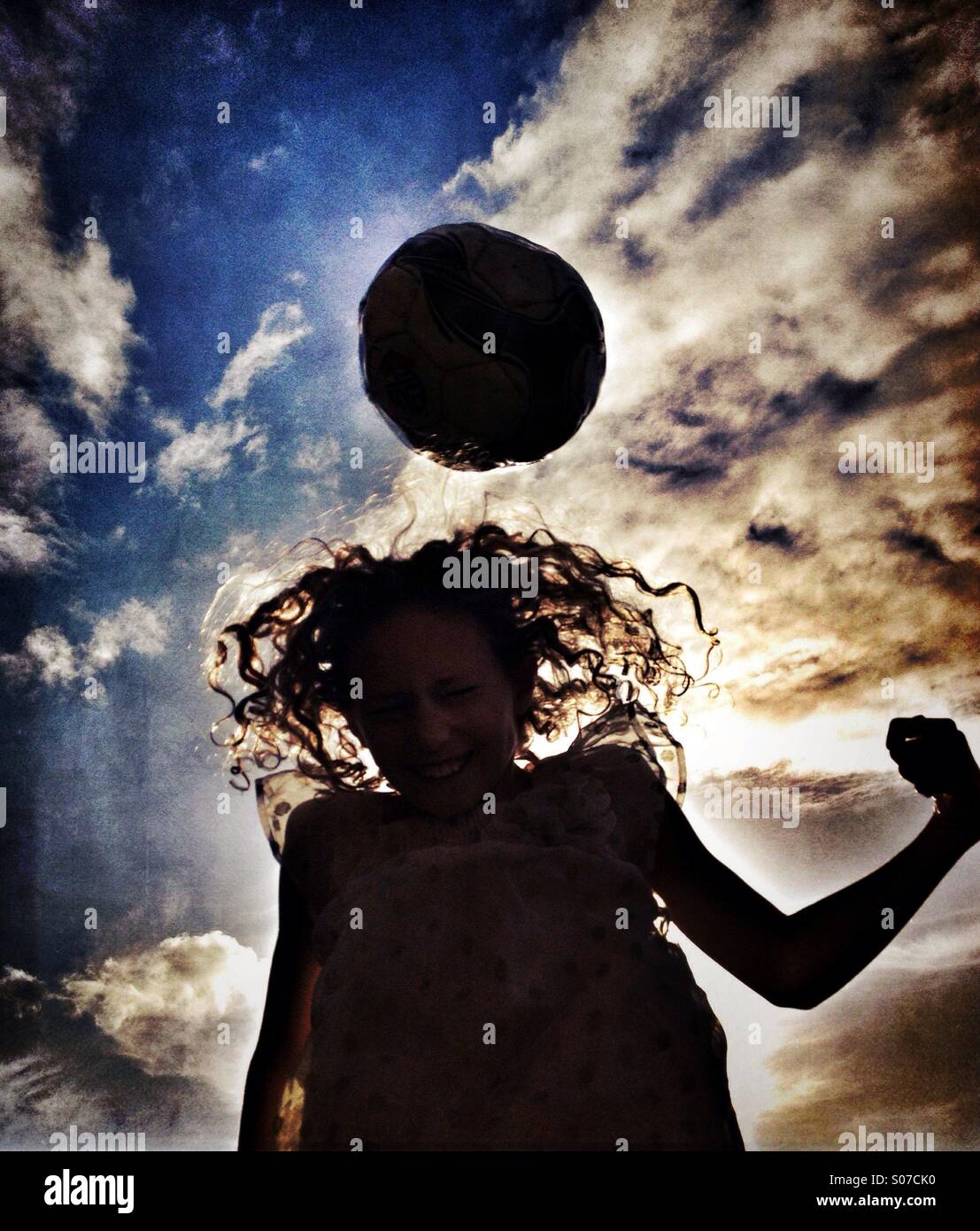 Girl heading football in silhouette against dramatic sky Stock Photo ...