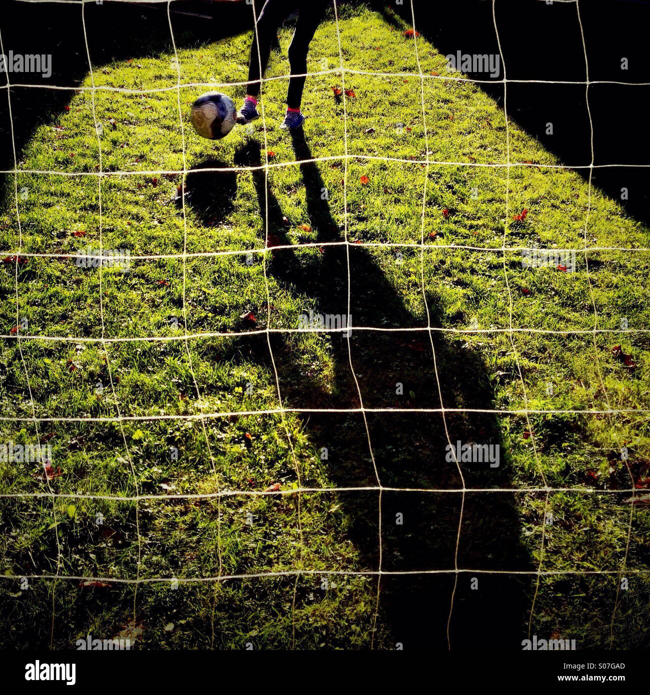 Young girl kicking football into net with long shadows Stock Photo - Alamy