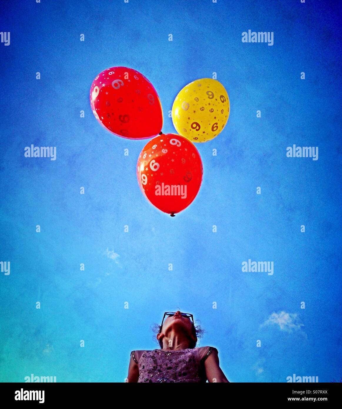 Girl blowing to keep three balloons up in air Stock Photo - Alamy