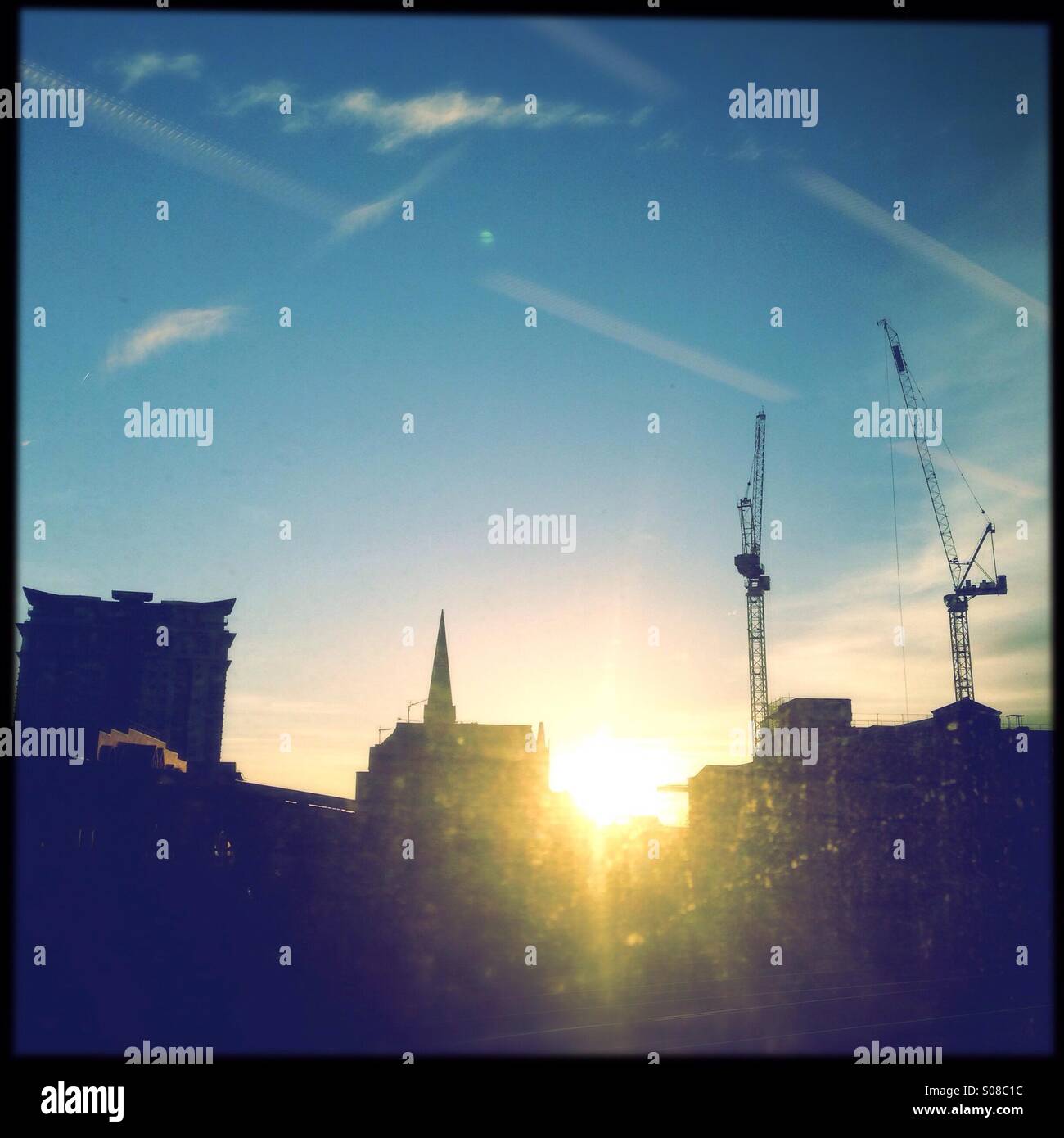 Sunrise between buildings and cranes; seen through a window Stock Photo ...