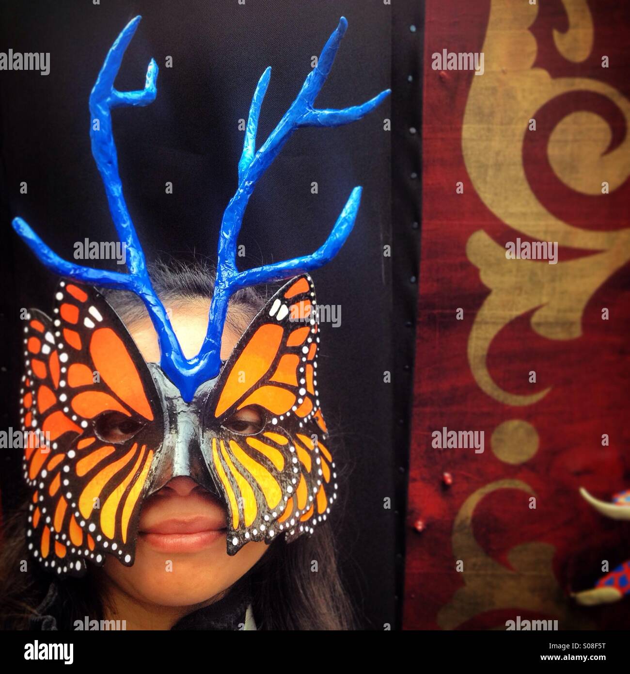 A girl wears a mask of a Monarch Butterfly with blue deer horns at the ...