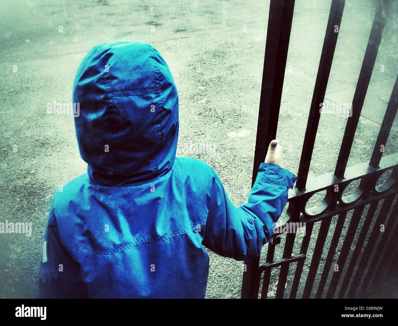 Little boy in blue coat waiting by the gate Stock Photo - Alamy