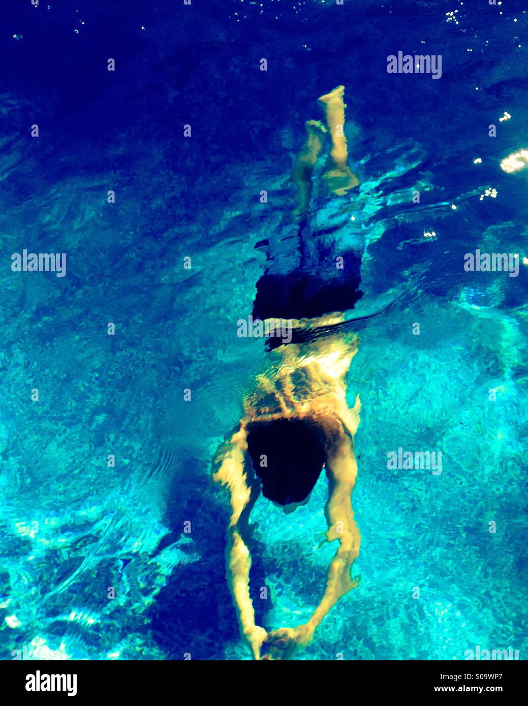 Young man swimming underwater in swimming pool as the sun glistens ...