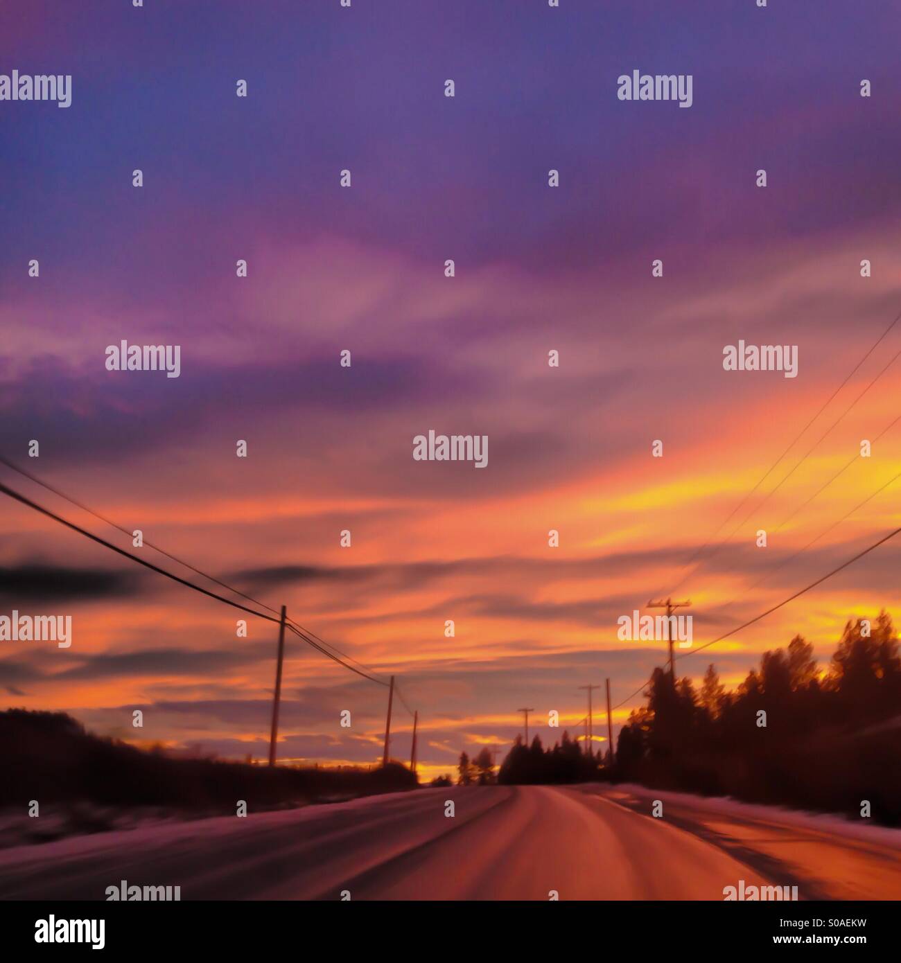 Driving into the sunset. The sunset covers the clouds and road below in ...