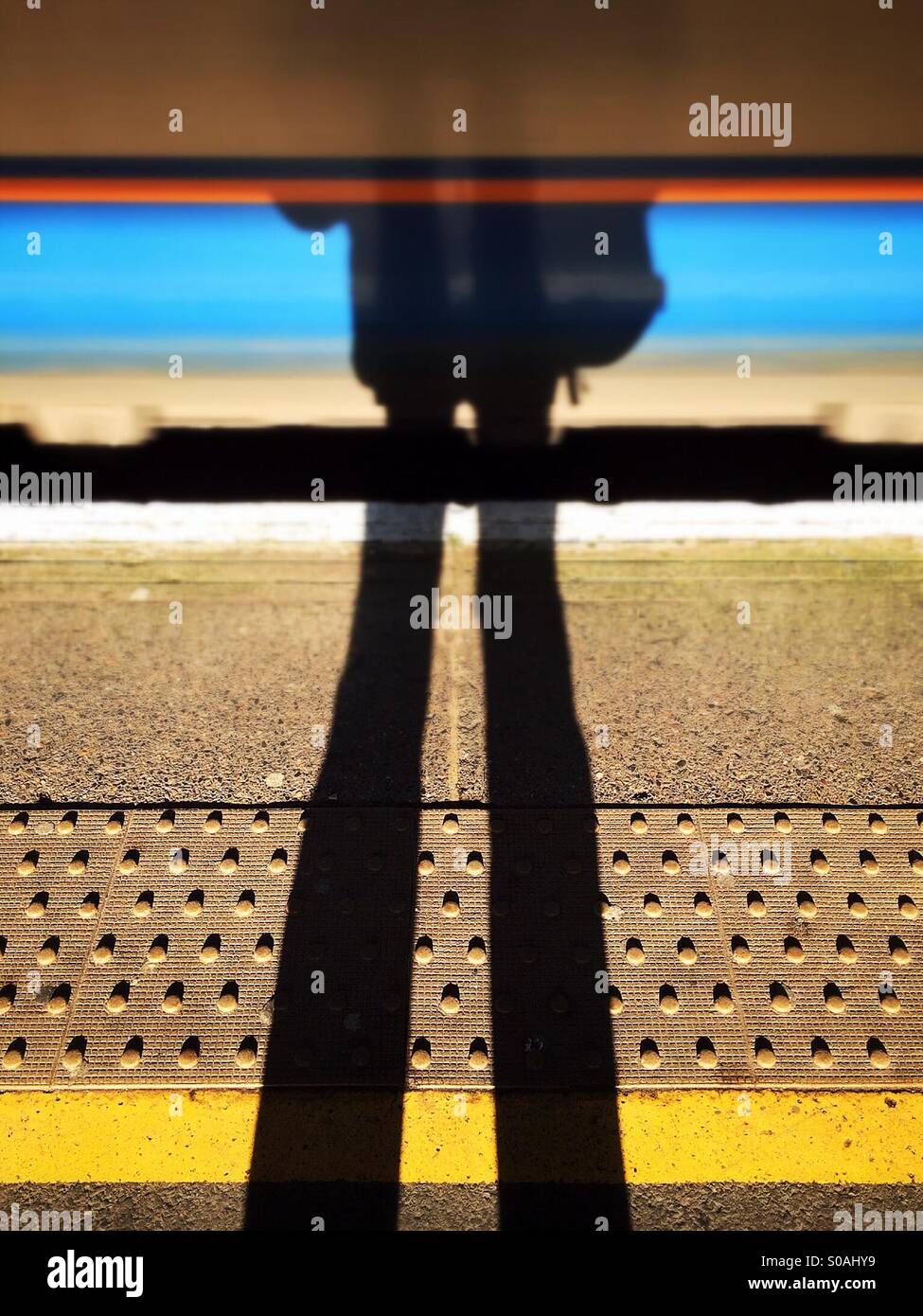 Shadow of a commuter waiting behind the yellow line on a railway ...