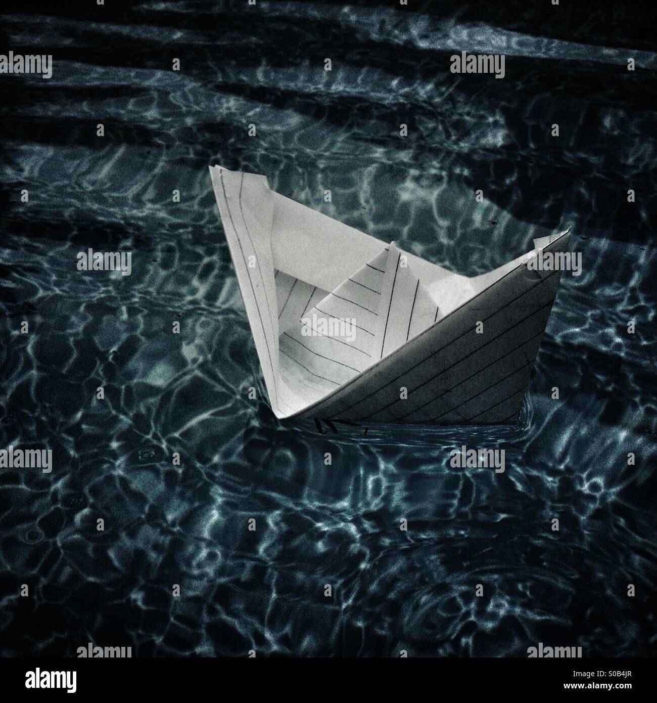 Paper boat made out of notebook page floating in swimming pool; dark ...