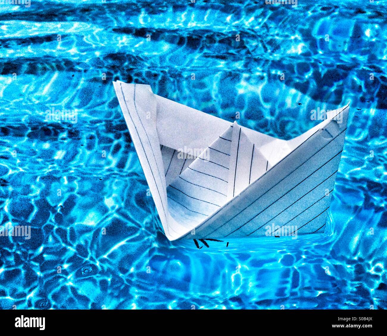 Paper boat folded from a notebook's page, floating on bright blue ...