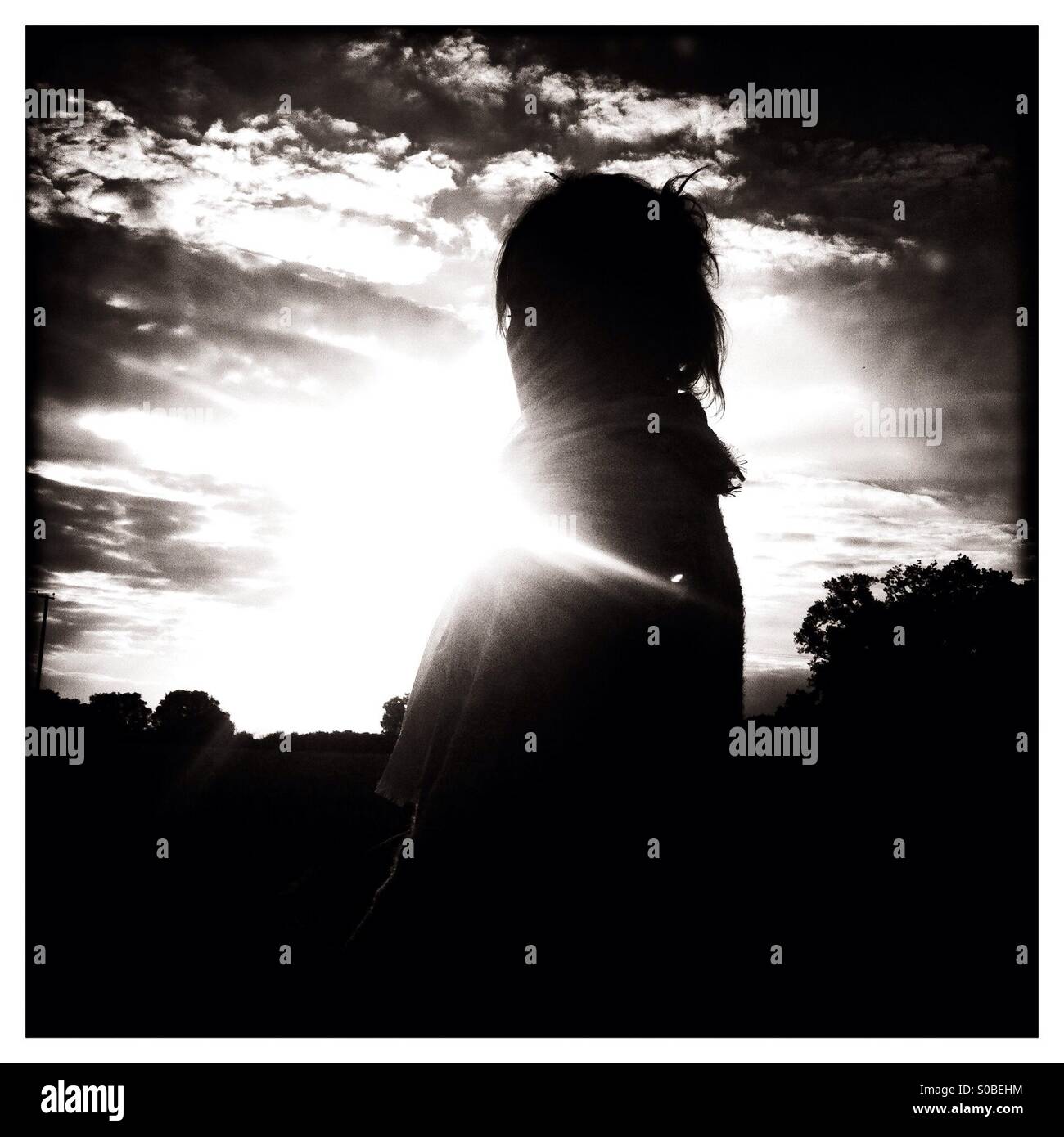 Girl looking into a sun low in a cloudy sky with a flare of sunlight on ...