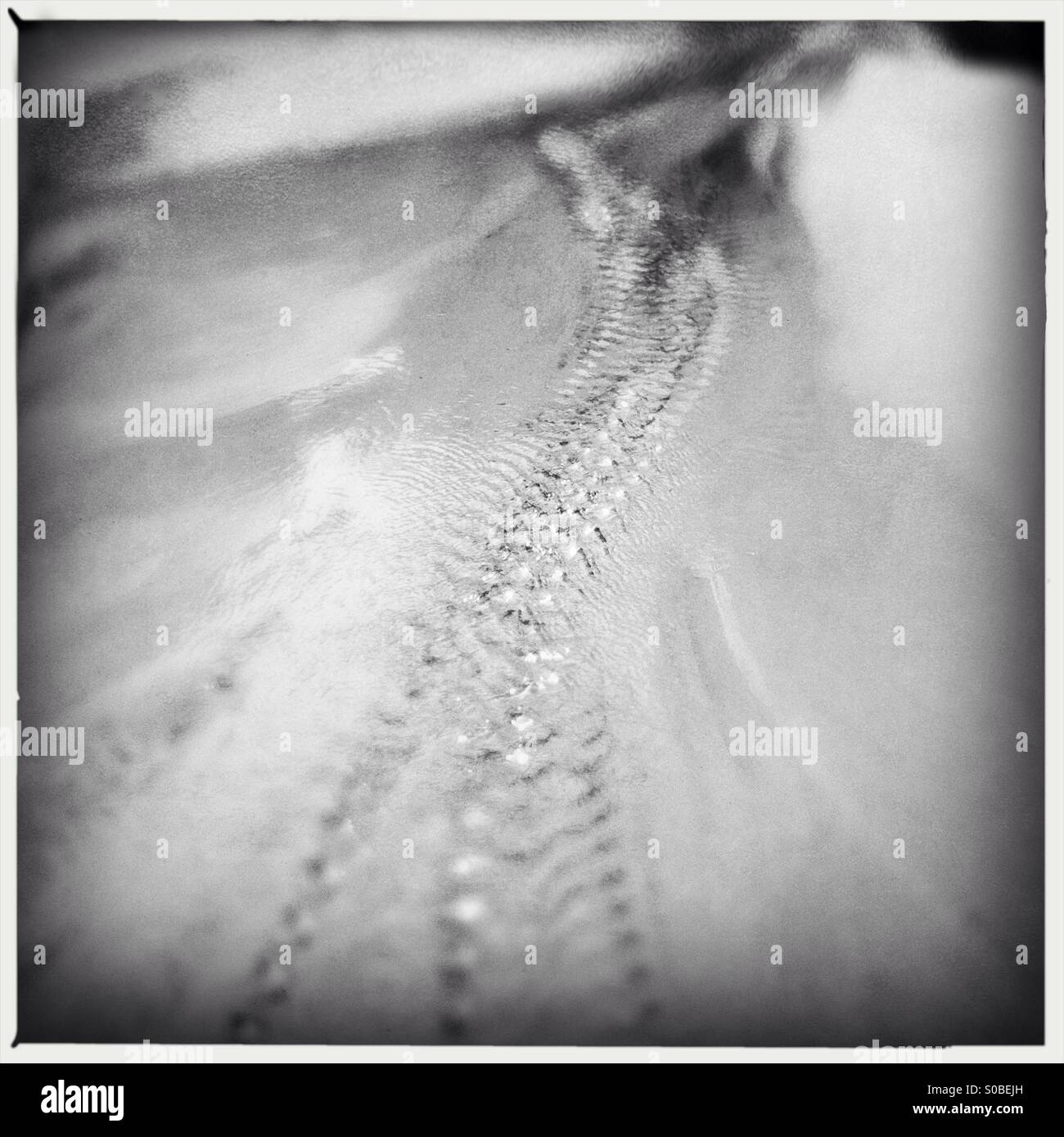 Stream of water trickling across sand on a beach, sparkling in the sun ...