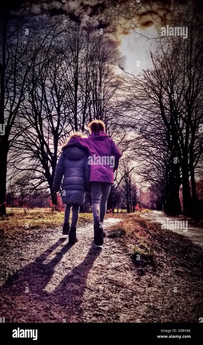 Sisters hugging walking down tree lined country path Stock Photo - Alamy