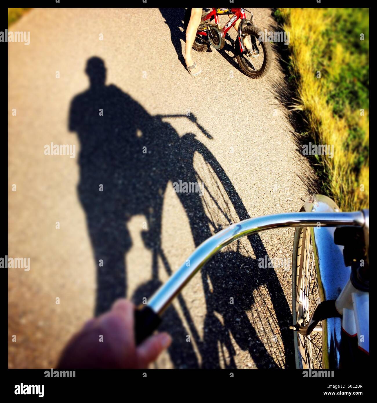 A shadow of a bike rider on a bike path talking to a child riding a ...