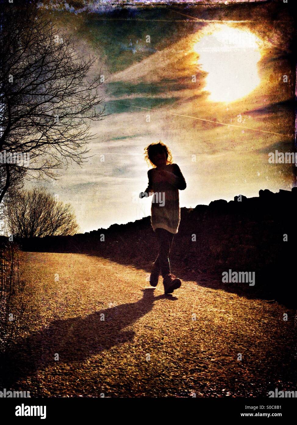 Young girl running along path backlit by sun Stock Photo - Alamy