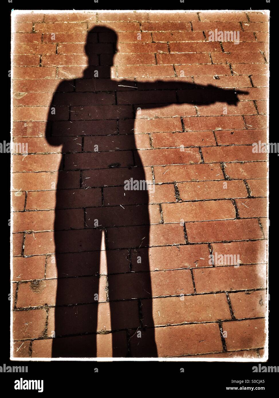 Shadow silhouette selfie of person pointing to the right, over brick ...