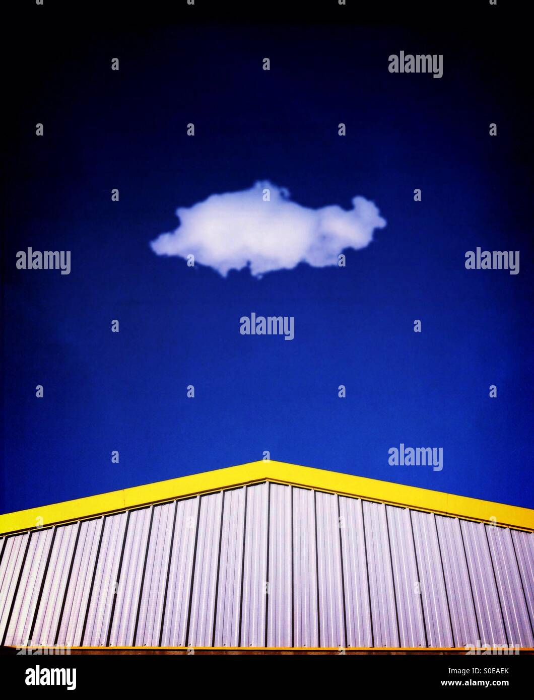 Yellow roof line of industrial building pointing at fluffy white cloud ...