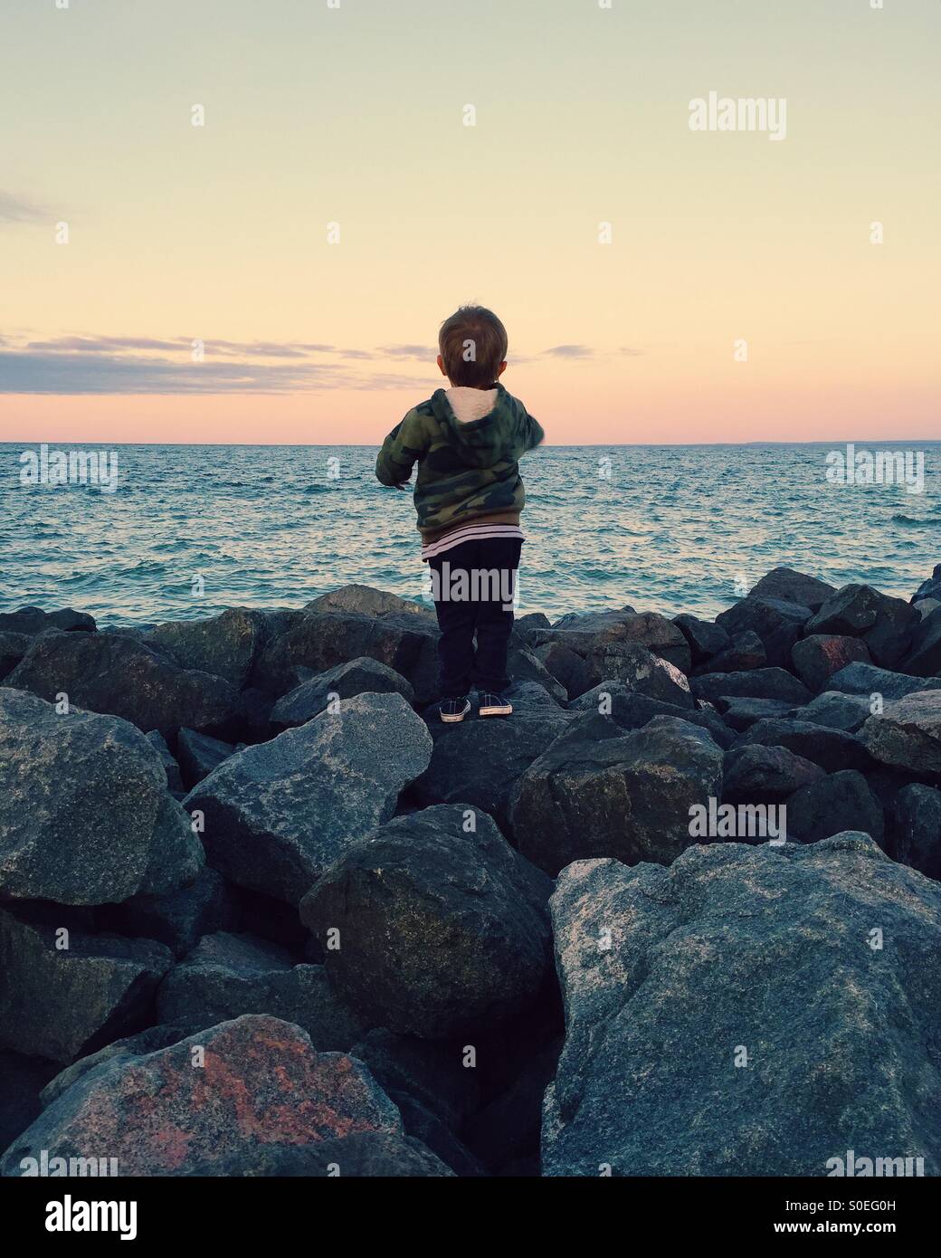 Child looking at sunset on shore Stock Photo - Alamy