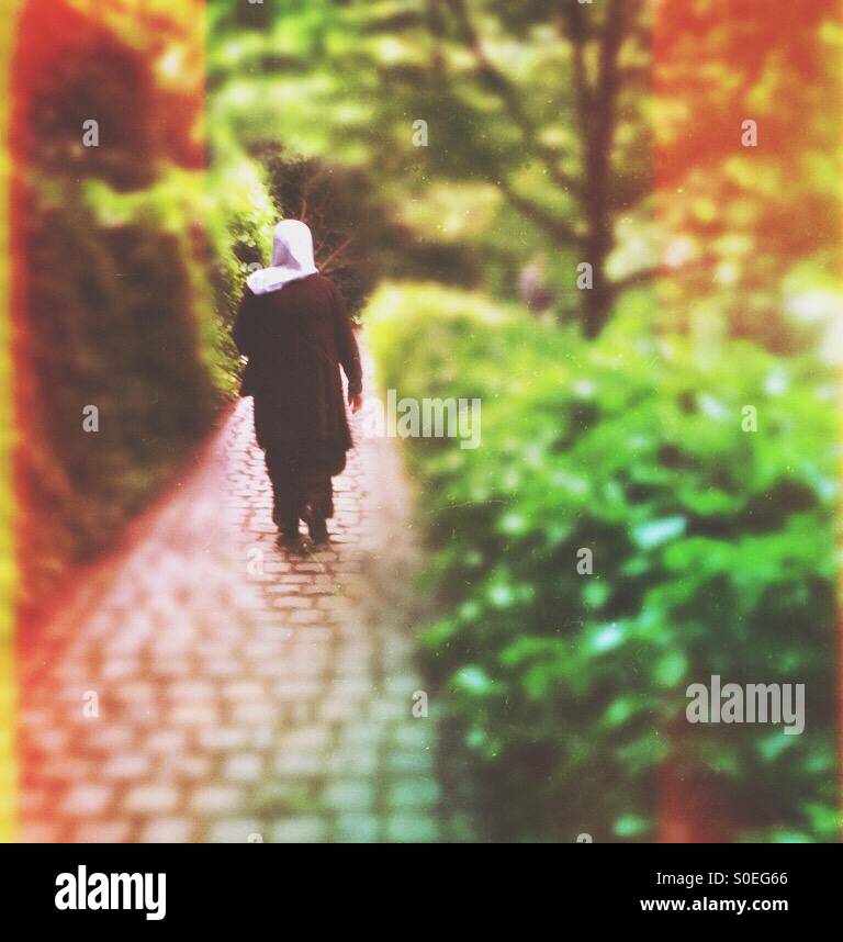 Old veiled woman walking on a cobblestone path in a park Stock Photo ...