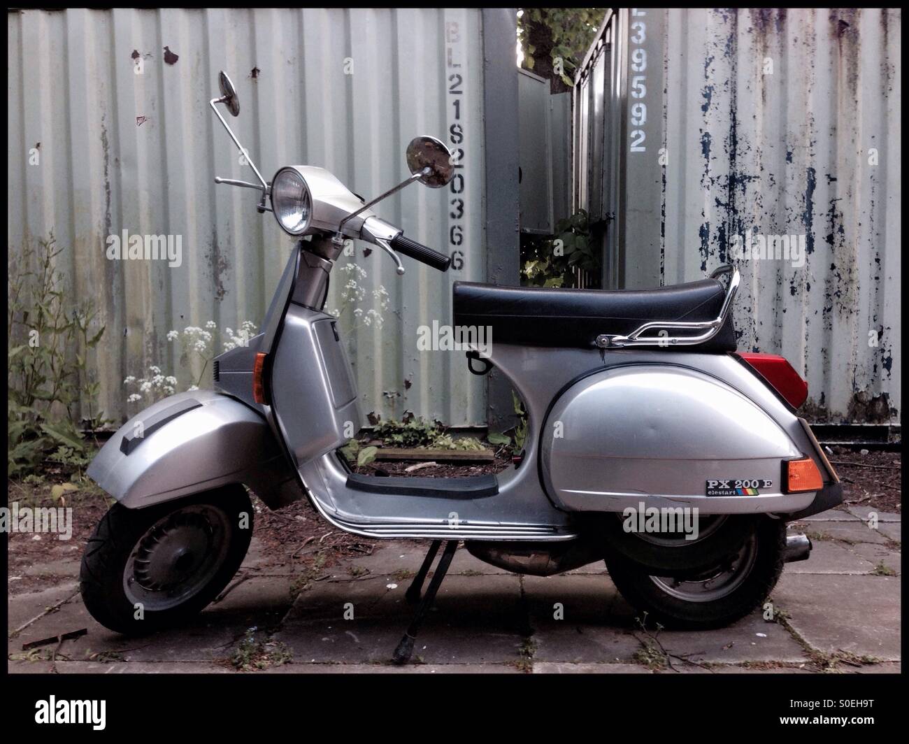 Vespa px200e motorbike or scooter parked against industrial containers in a casual outdoor ...