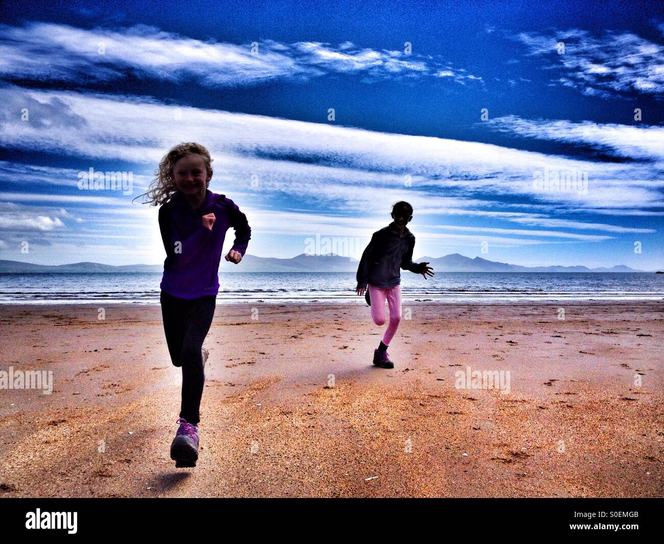 Two young girls running on Newborough beach on Anglesey in North Wales ...