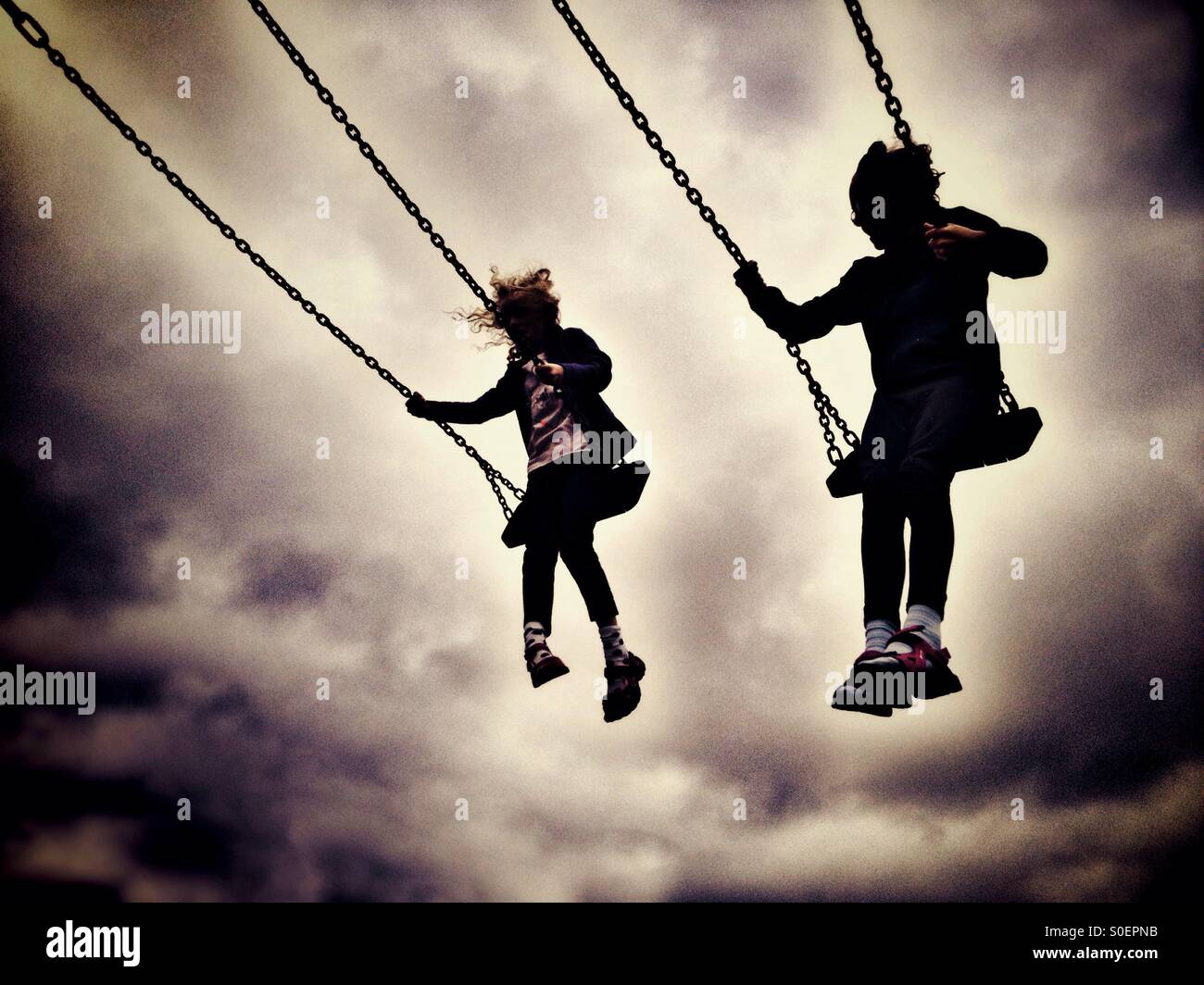 Two girls on swings in silhouette against cloudy sky Stock Photo - Alamy