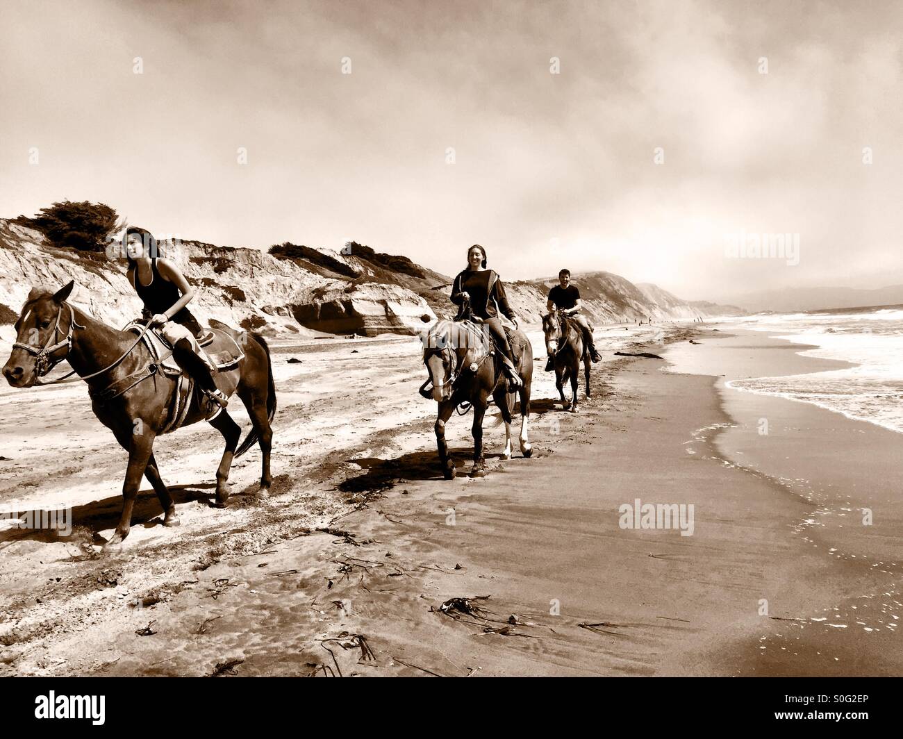 Three riders on horseback appear out of a long stretch of California ...