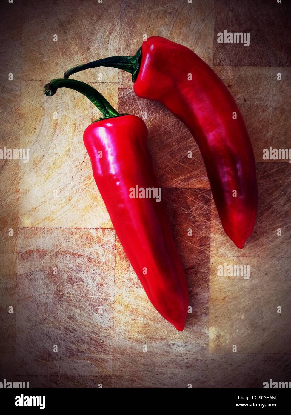 Digitally enhanced photograph of two red chillies on a chopping board ...