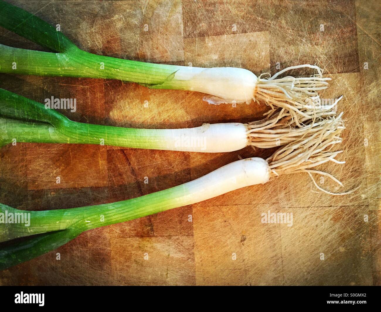 Three spring onions on a chopping board Stock Photo - Alamy