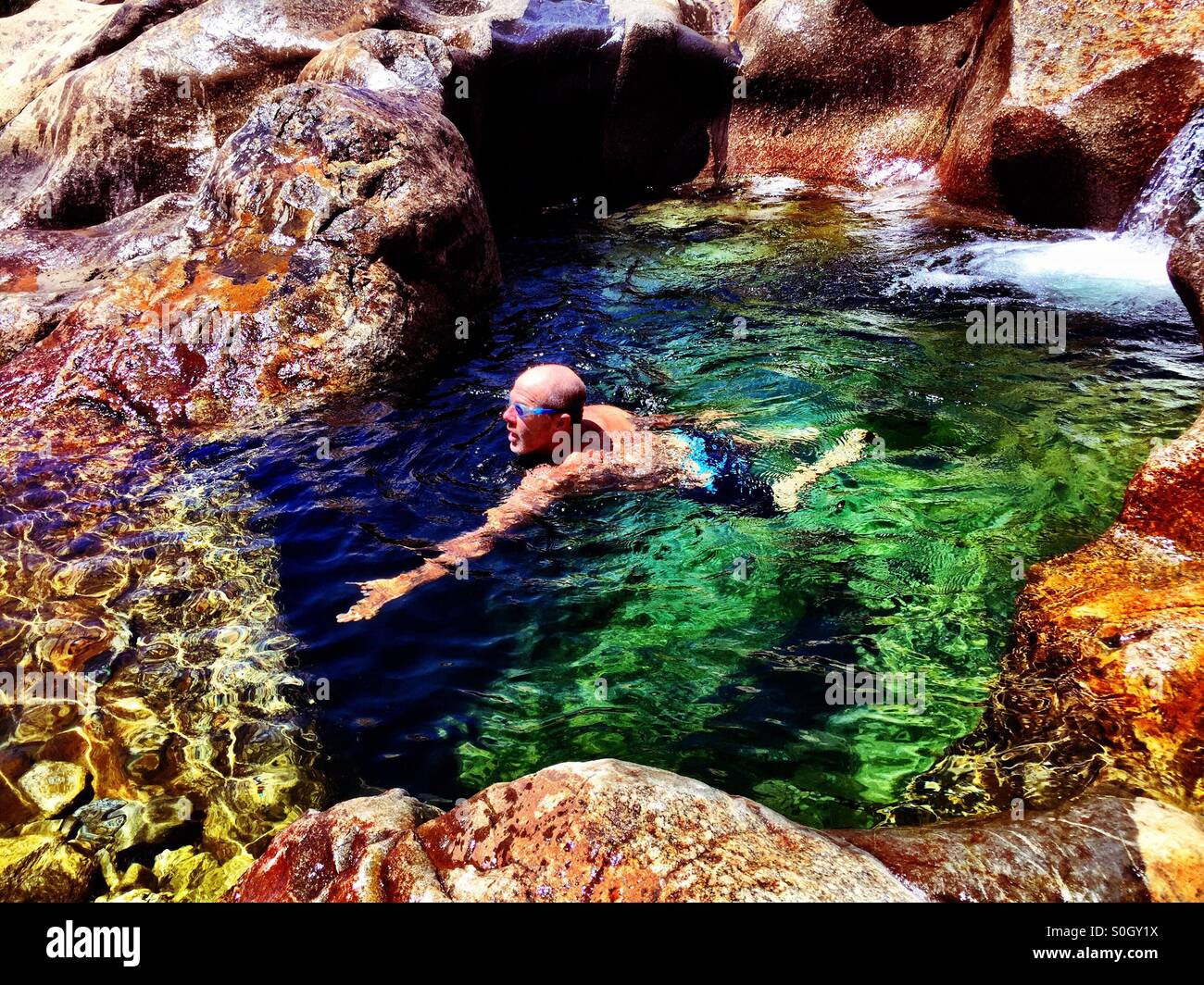 Swimming under a waterfall in a naturally formed pool in the mountain ...