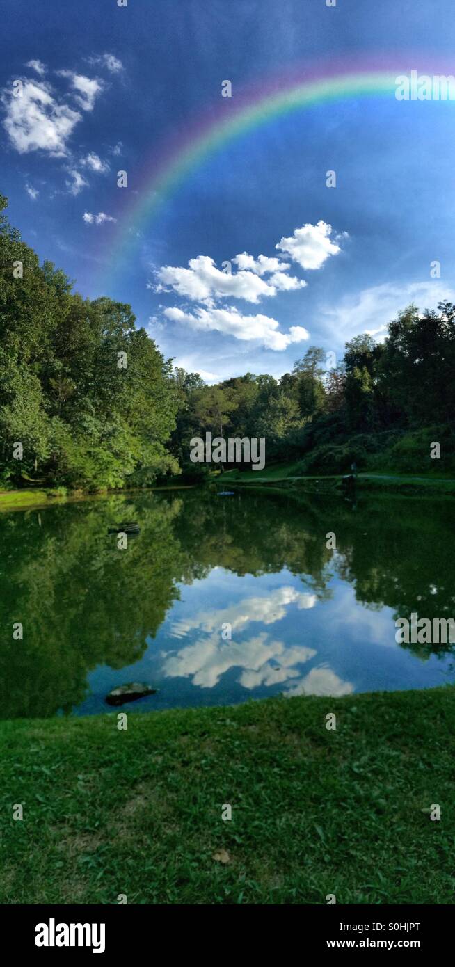A rainbow in a beautiful blue sky with clouds reflected in a lake Stock ...