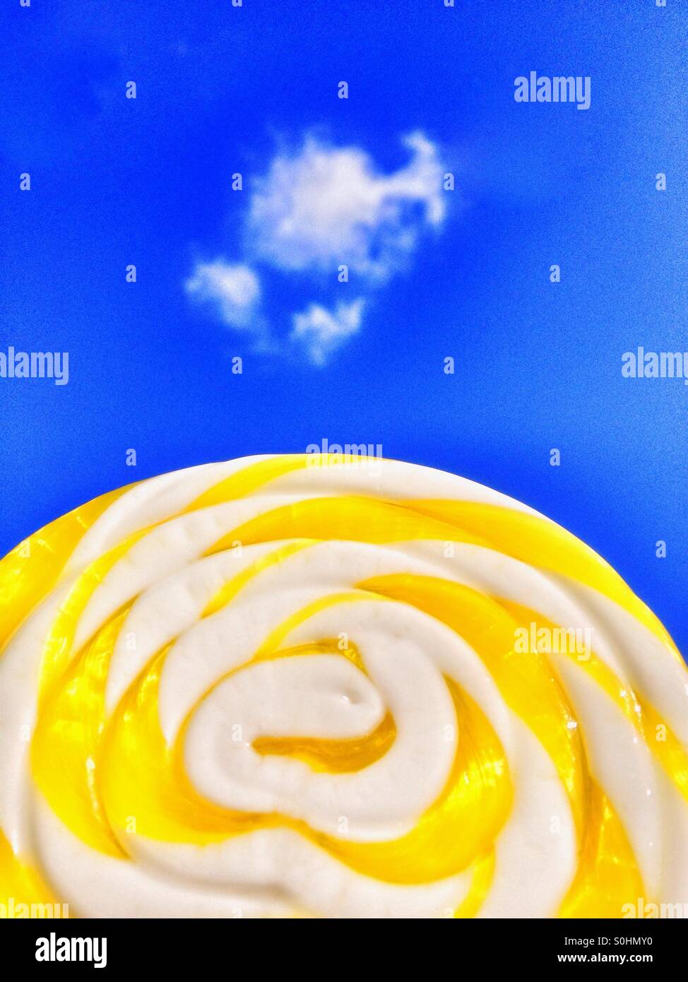 Yellow and white candy lolly against a blue sky with fluffy white cloud ...