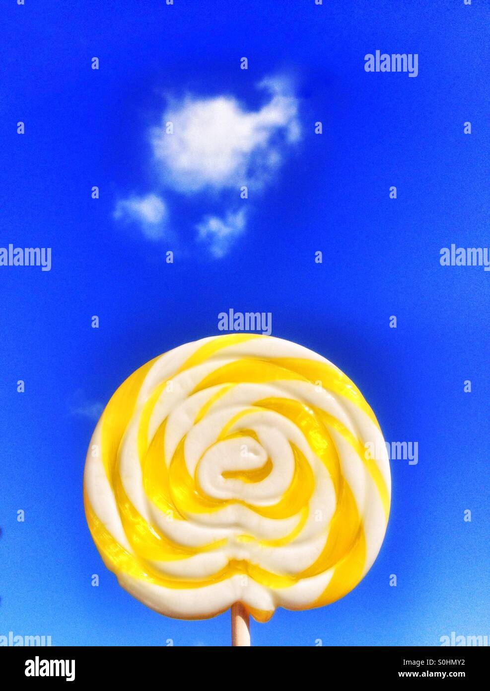 Yellow and white candy lolly against a blue sky with fluffy white cloud ...