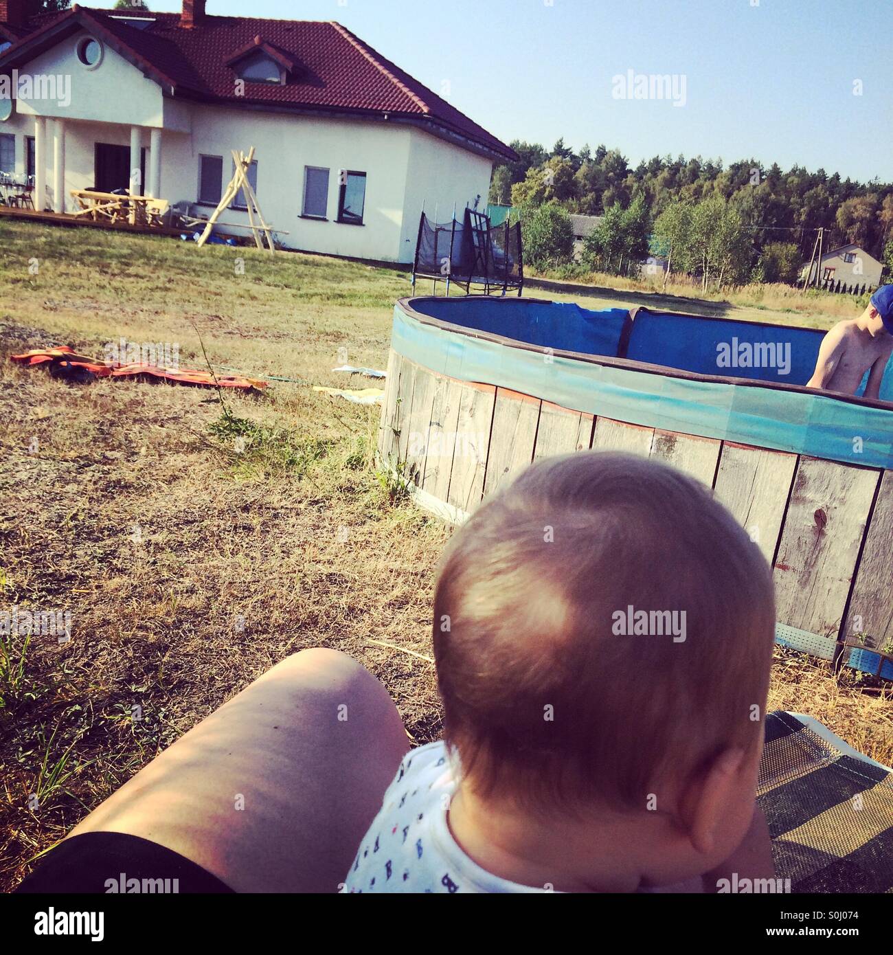 Baby watching his brother in the pool and the house Stock Photo - Alamy
