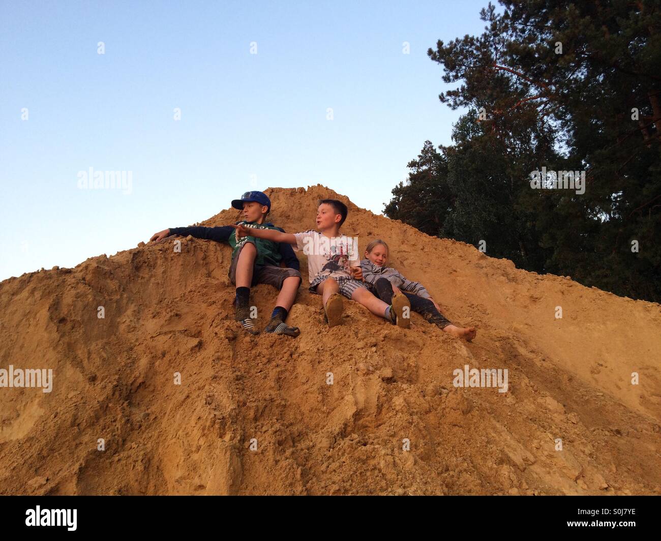 Three kids sitting on a sand pile Stock Photo - Alamy