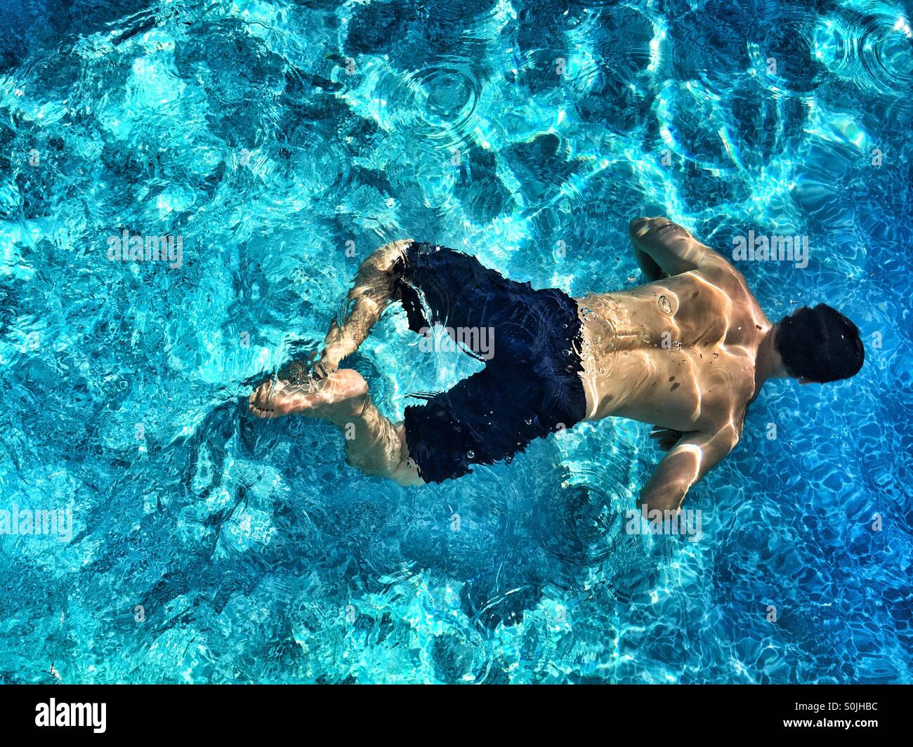 Young man swimming underwater in outdoor swimming pool on a sunny day ...
