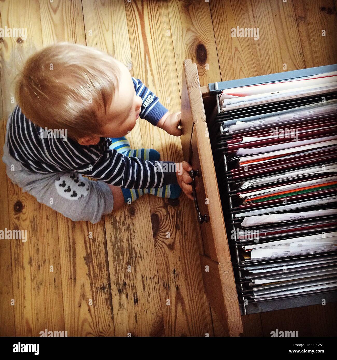 8 months old baby boy sitting on a wooden floor and playing with an ...