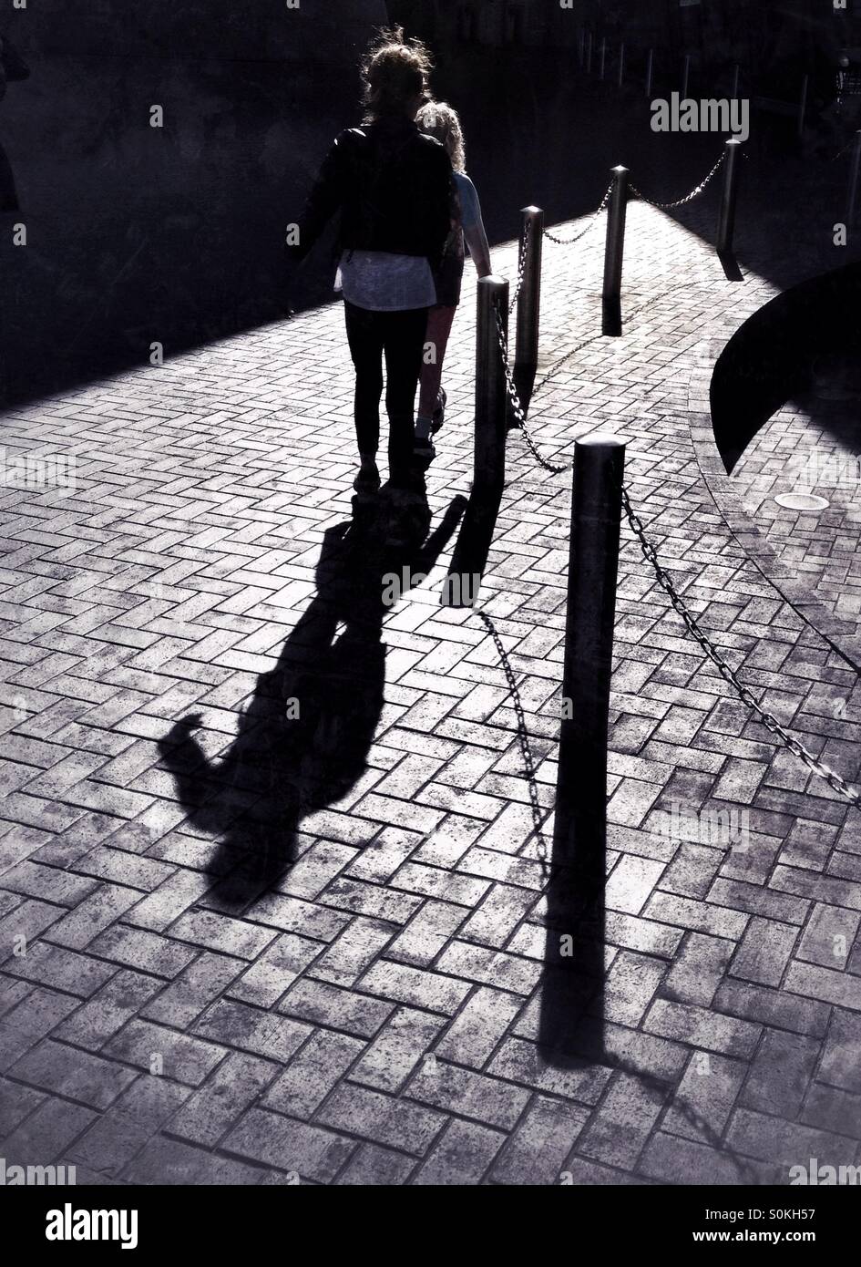 Two young children casting shadows on paved path by bollards Stock ...