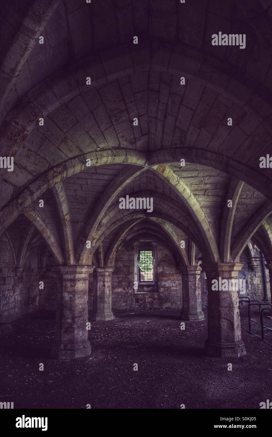 Dark and gloomy church catacombs with a single, barred window and dimly ...