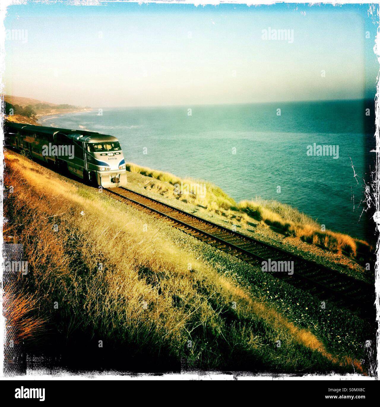 Square color photo of passenger train traveling up the ocean coastline ...
