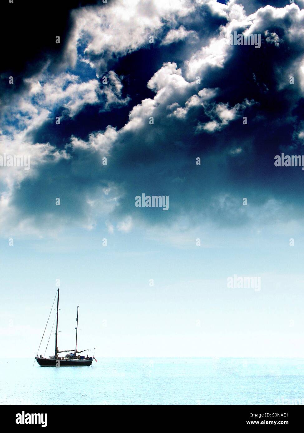 A solitary yacht on a calm sea below a foreboding black cloud. Ice ...