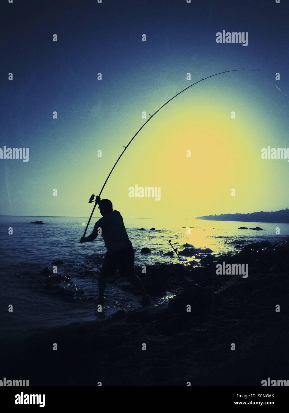 Man sea fishing at sunset Stock Photo - Alamy