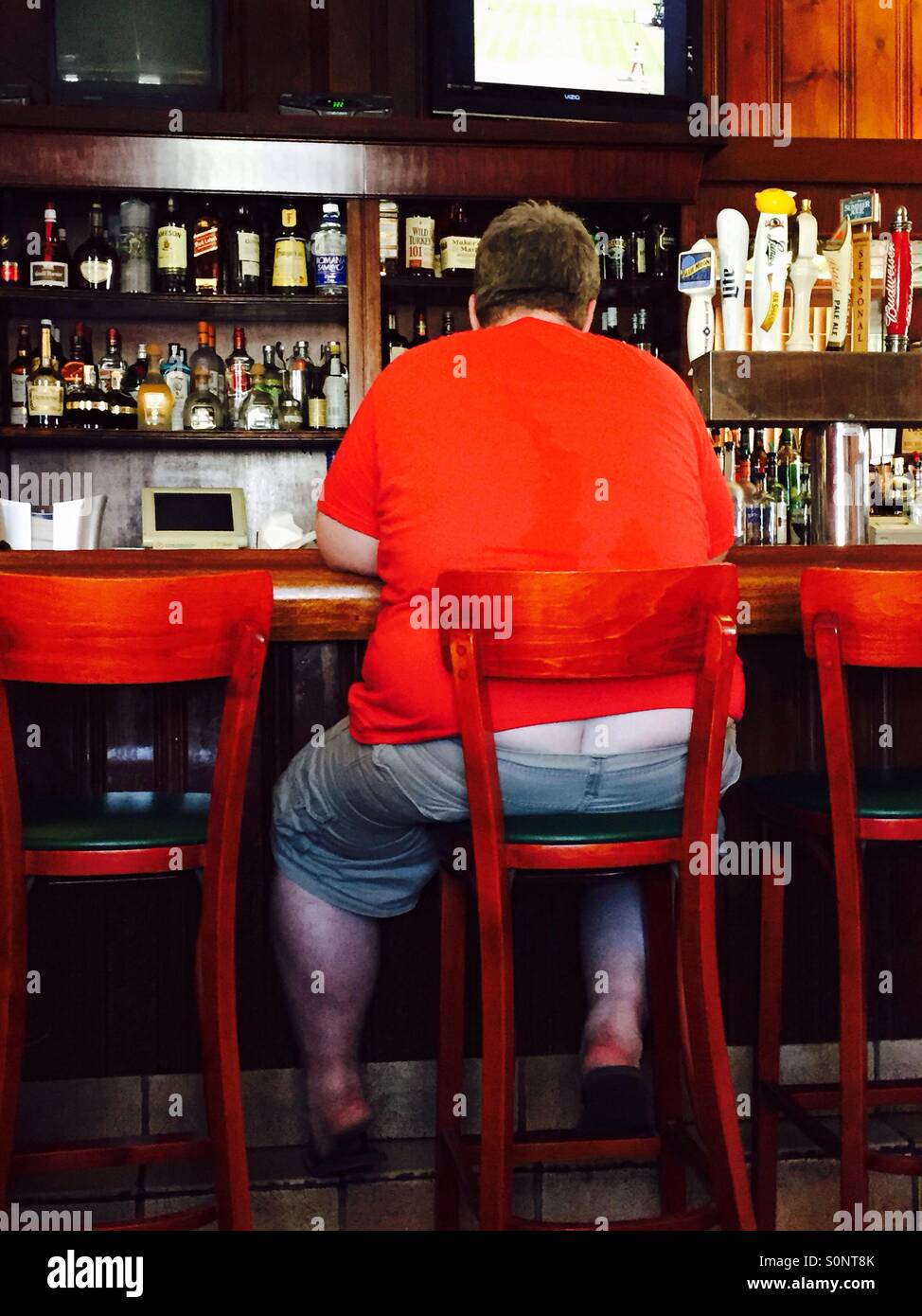 Overweight man sitting on chair in a bar, rear view Stock Photo - Alamy