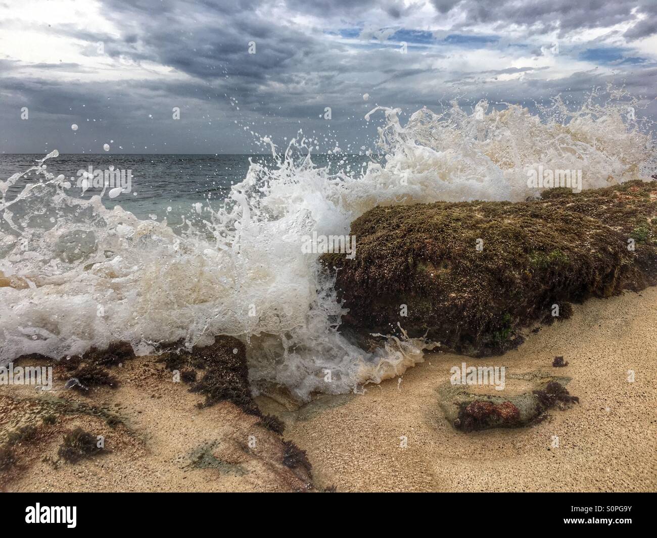Waves crashing over rocks on a sandy beach Stock Photo - Alamy